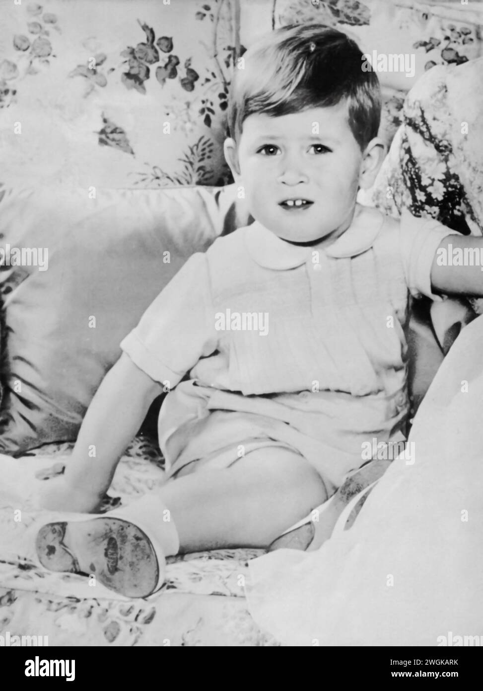 A young Prince Charles III is shown seated comfortably on a sofa, circa ...