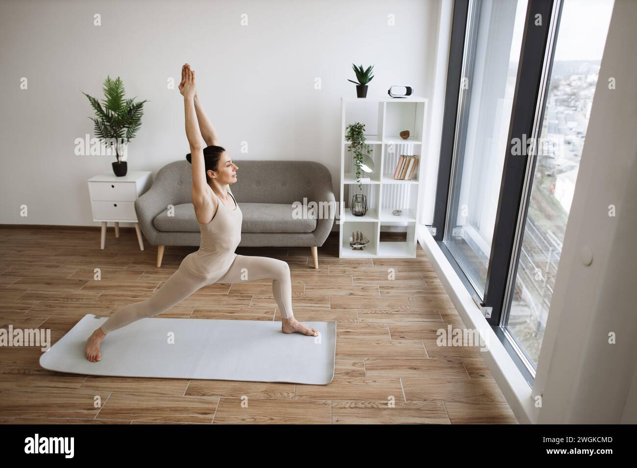 Mature brunette practising Warrior One Pose during yoga exercise at ...