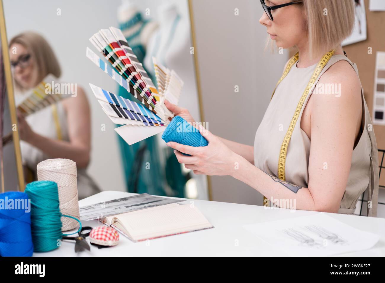 Fashion designer holds thread coil and color swatch fan in dressmaking ...