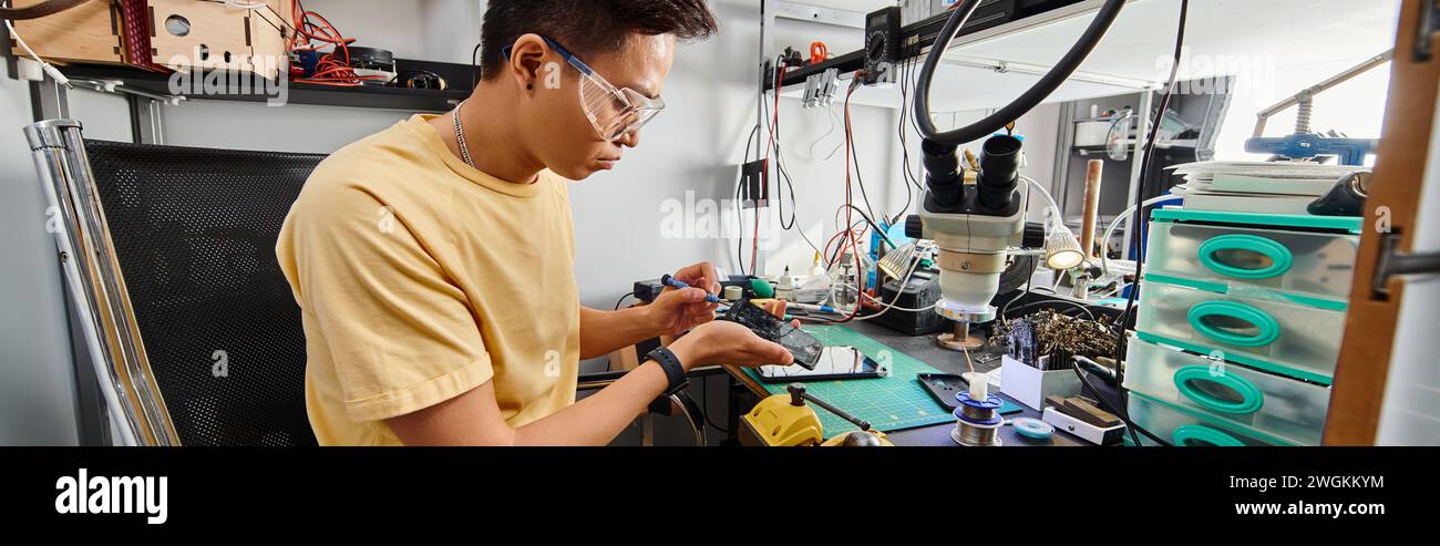 skilled asian technician in goggles working with electronic devices in ...