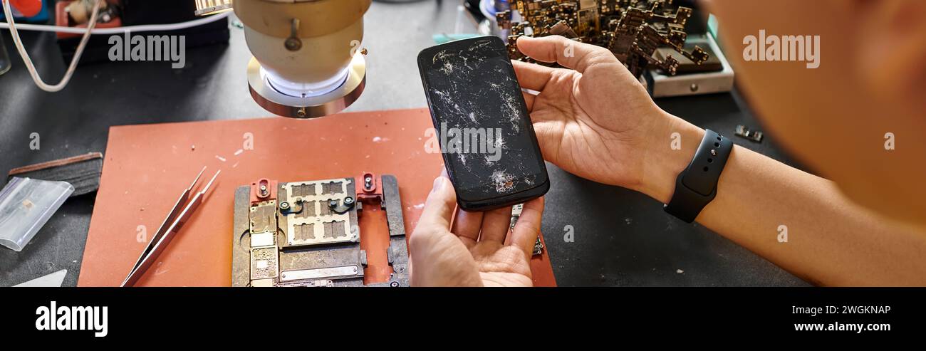 cropped view of skilled repairman holding mobile phone with broken ...