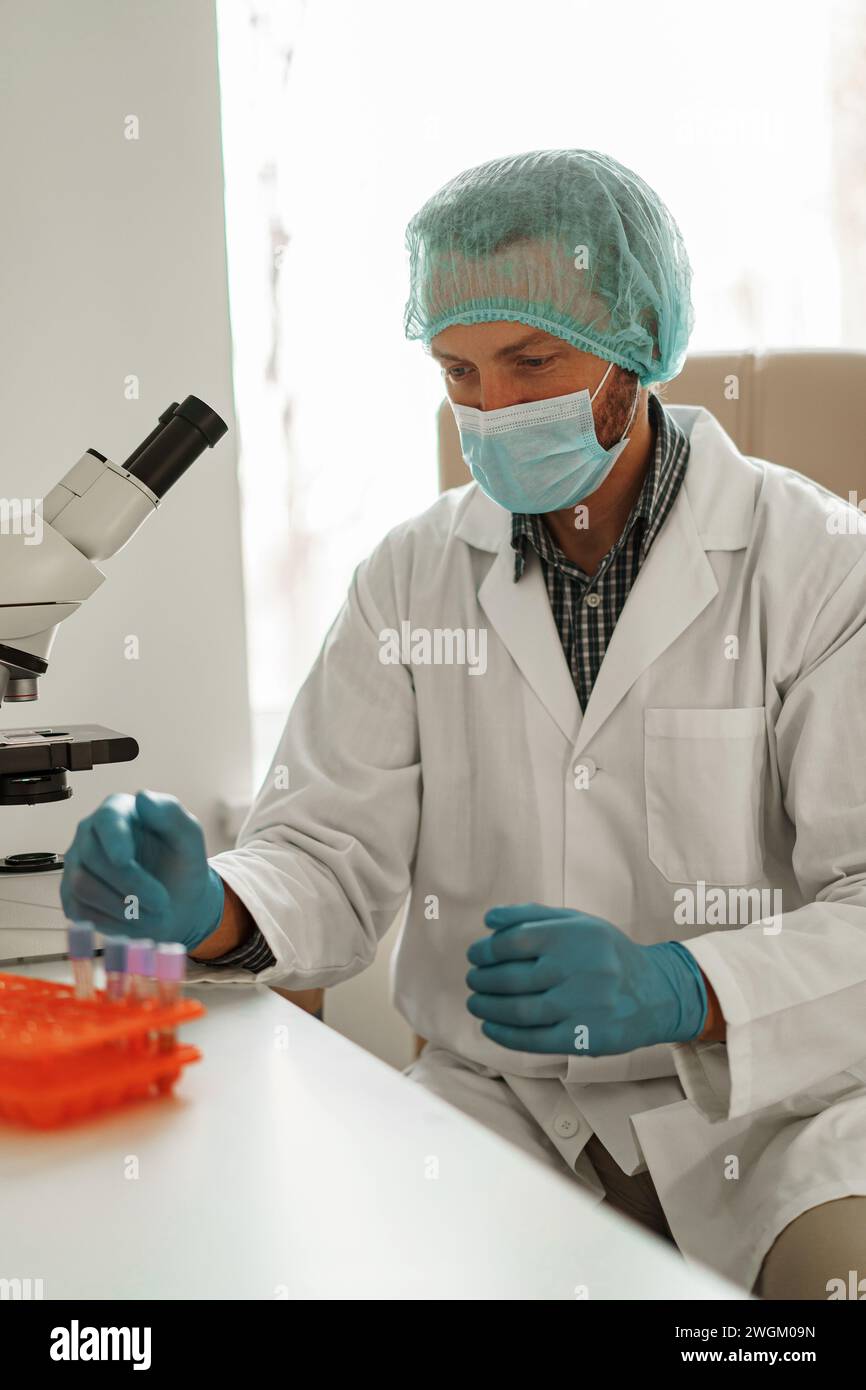 Male scientist looking under microscope does analysis of test sample in ...
