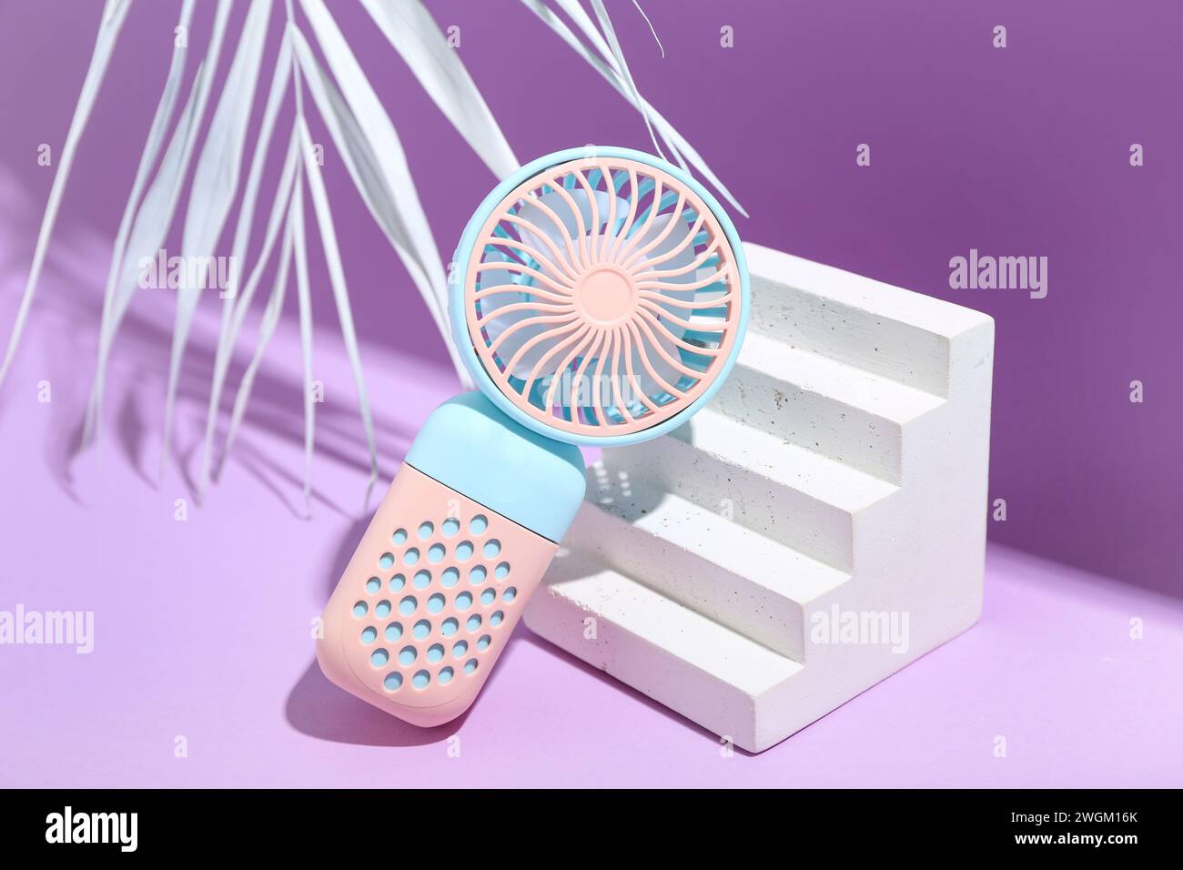 Plaster podium with portable electric fan and palm leaf on purple ...