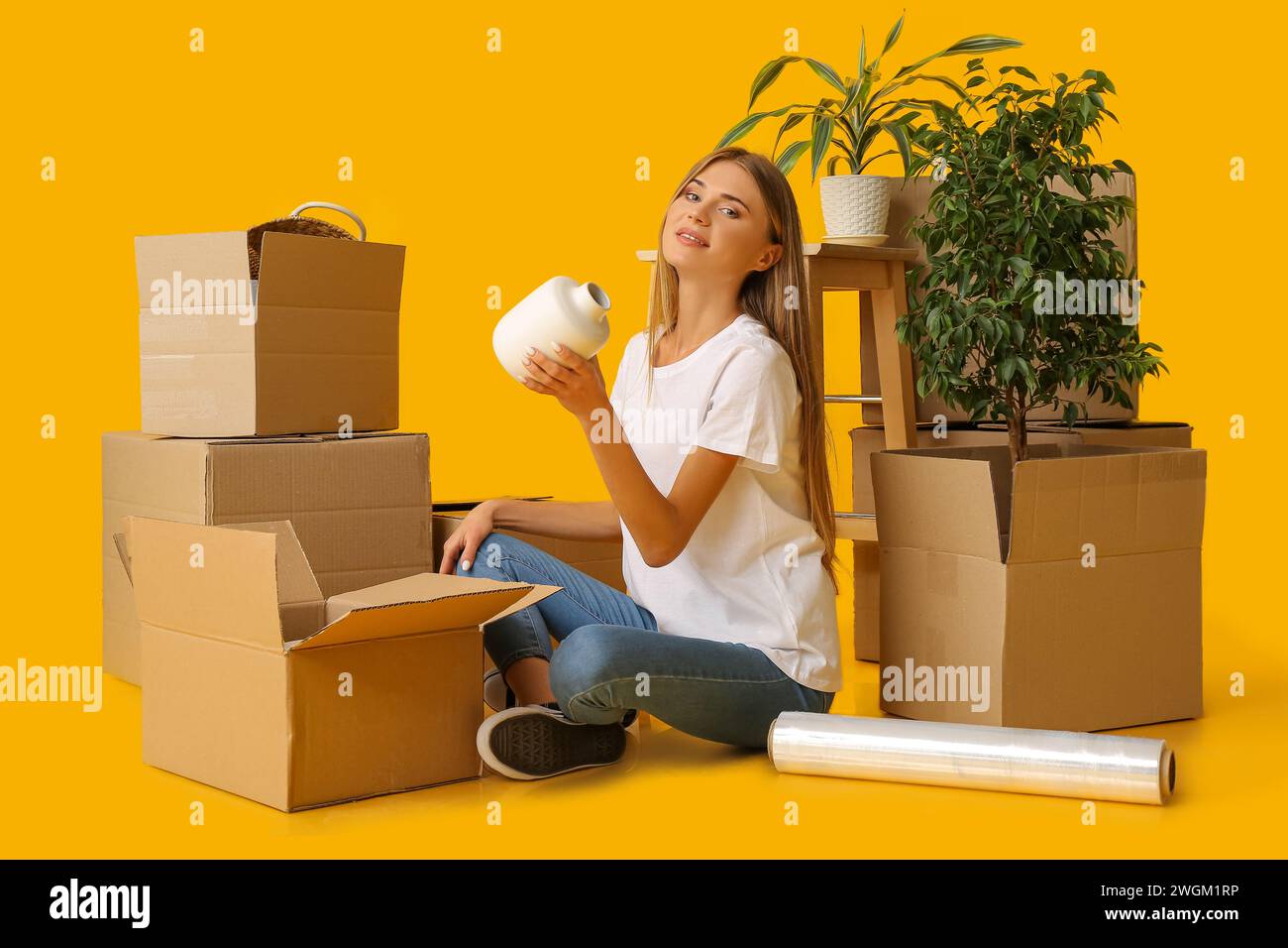 Pretty young woman packing her belongings in cardboard boxes on yellow ...