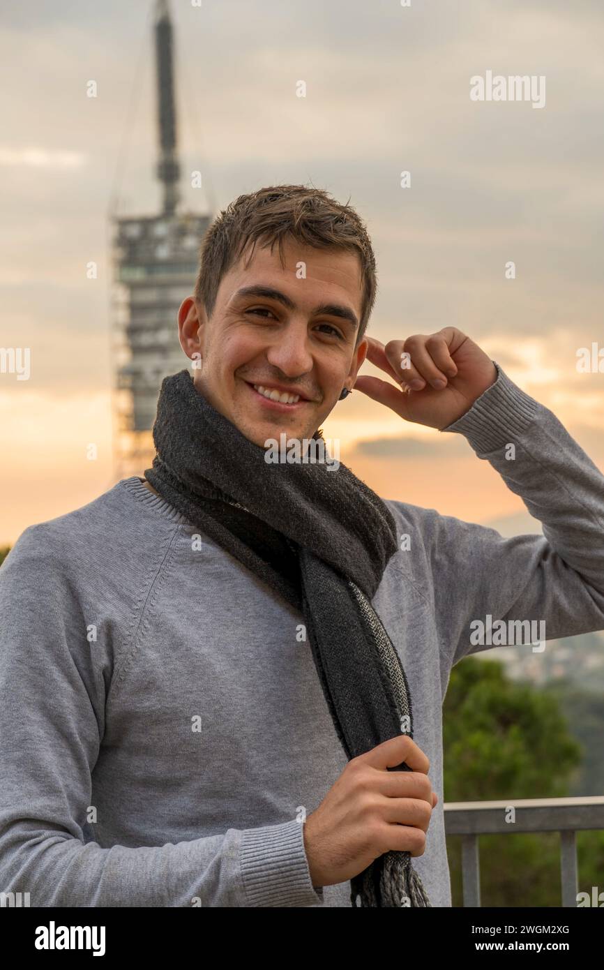 Young brown haired man smiling at the camera while touching his ear ...