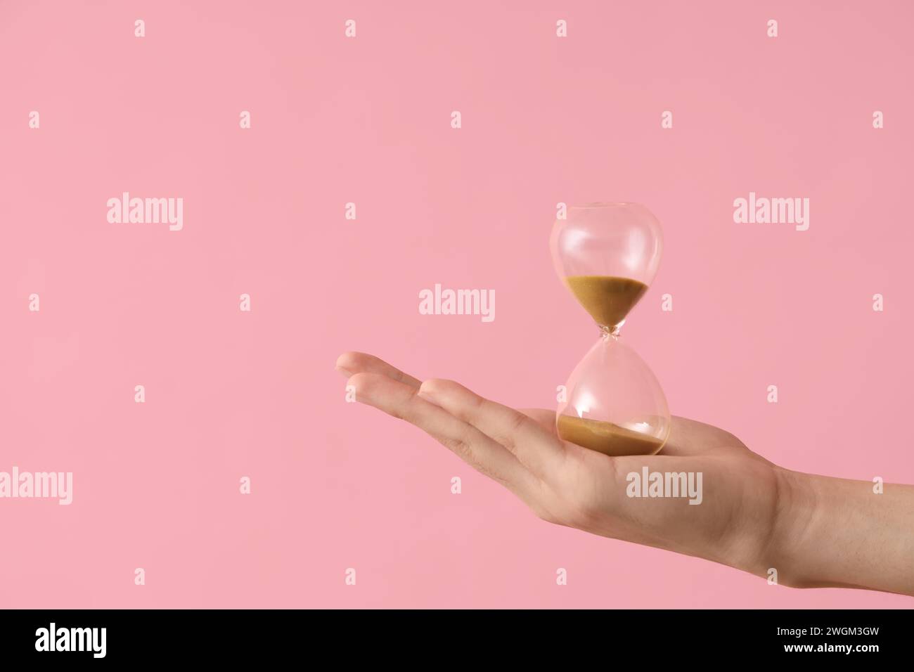 Female hand holding hourglass on pink background Stock Photo - Alamy