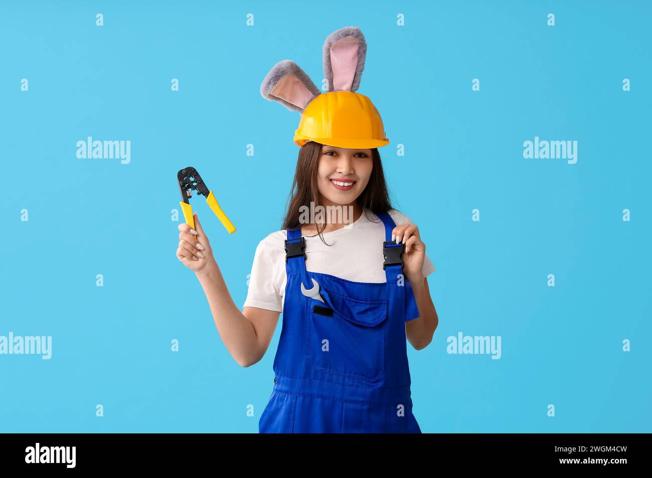 Female Asian worker in bunny ears with pliers on blue background ...