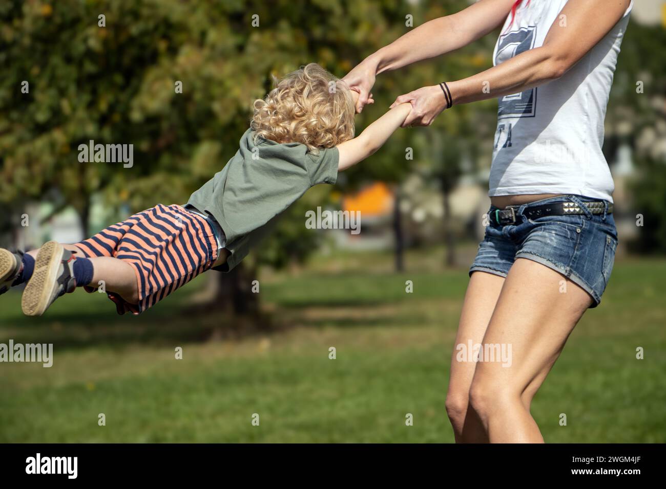 A young woman turns little boy in circle. Mom and son playing circling around Stock Photo - Alamy