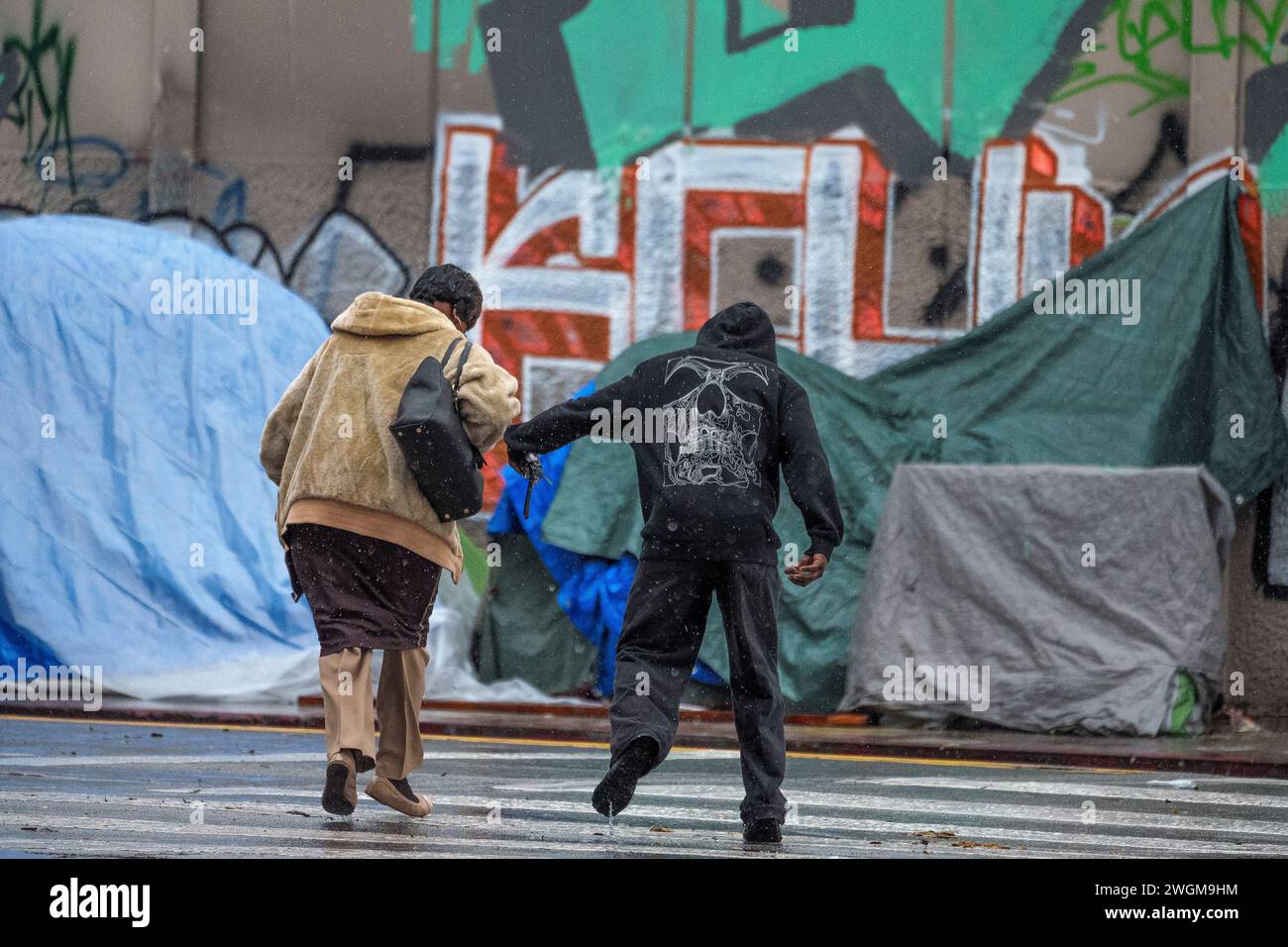 People cross the street under heavy rain in the Skid Row area, one of ...
