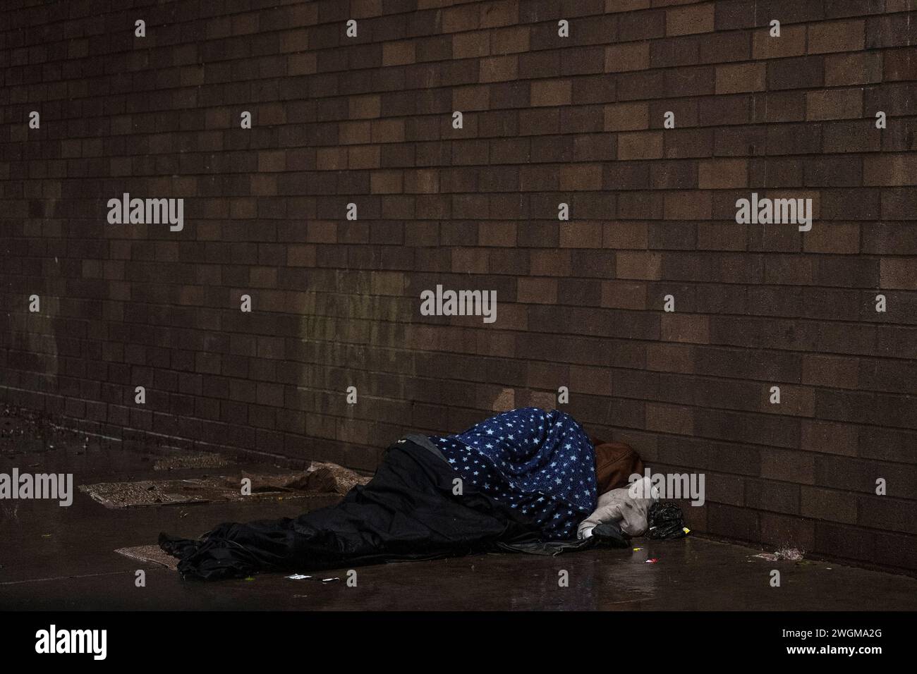 A person suffering from homelessness sleeps on the sidewalk covered ...