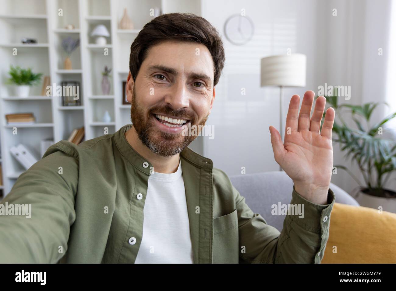 Adult male with stylish hairstyle waving hello with hand to camera ...
