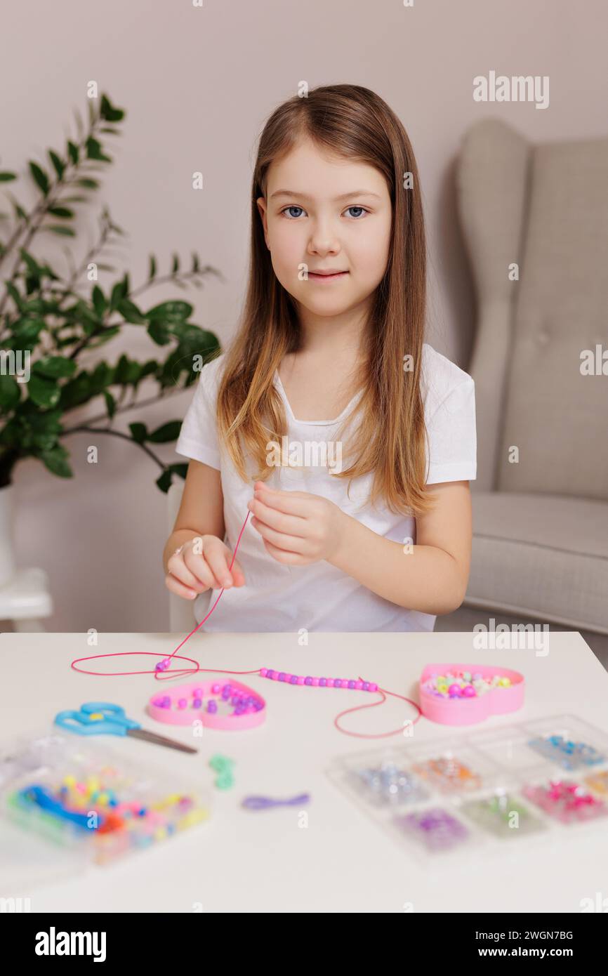 Girl making beaded jewelry at table in room Stock Photo - Alamy
