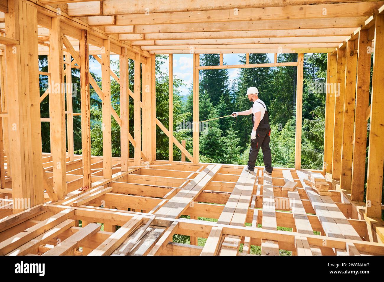 Carpenter is constructing wooden frame house. Man taking measurements ...