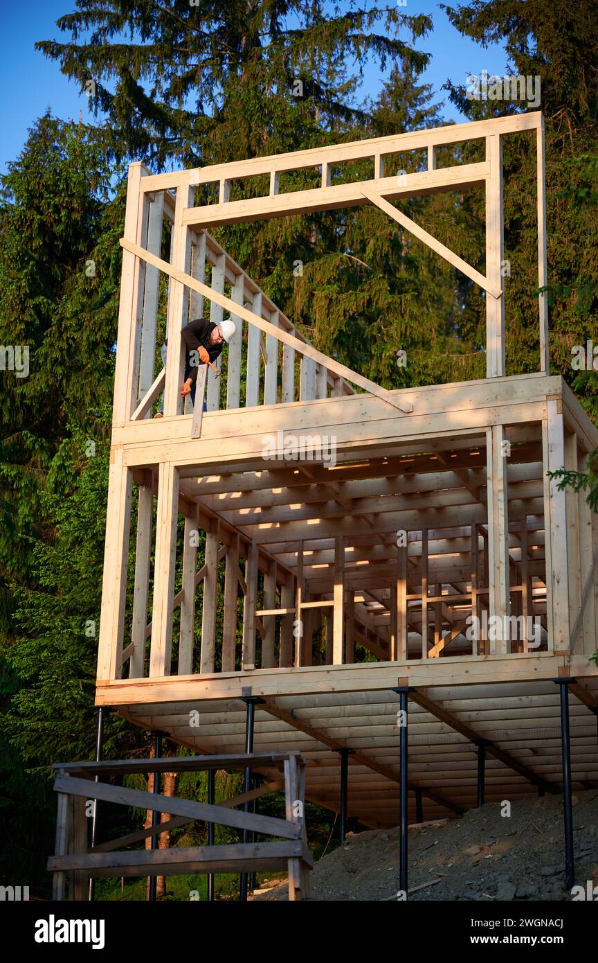 Carpenter constructing wooden two-story frame house close to the woods ...