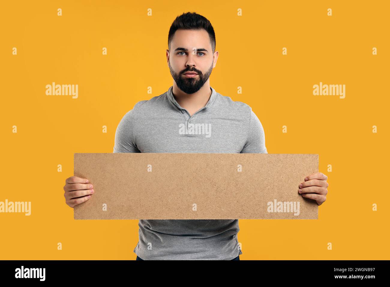 Man holding blank cardboard banner on orange background, space for text ...