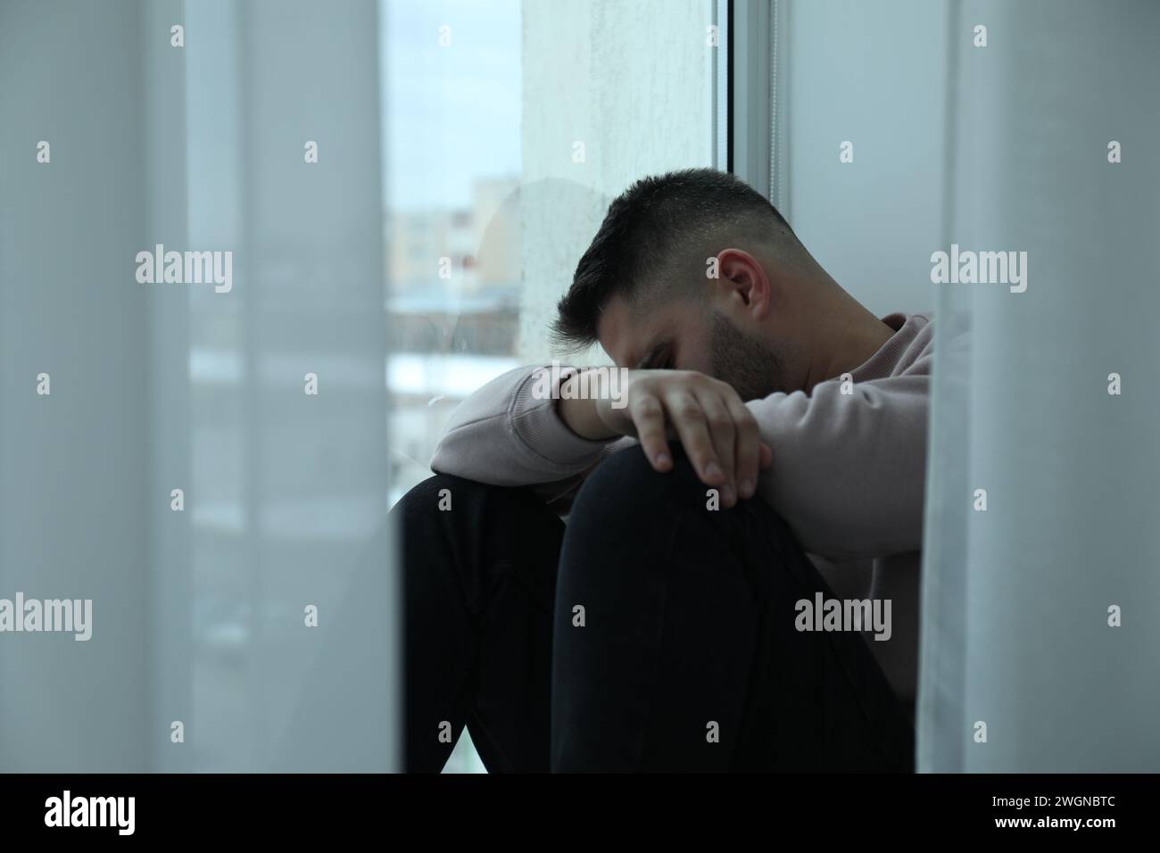 Sad man sitting near window at home Stock Photo - Alamy
