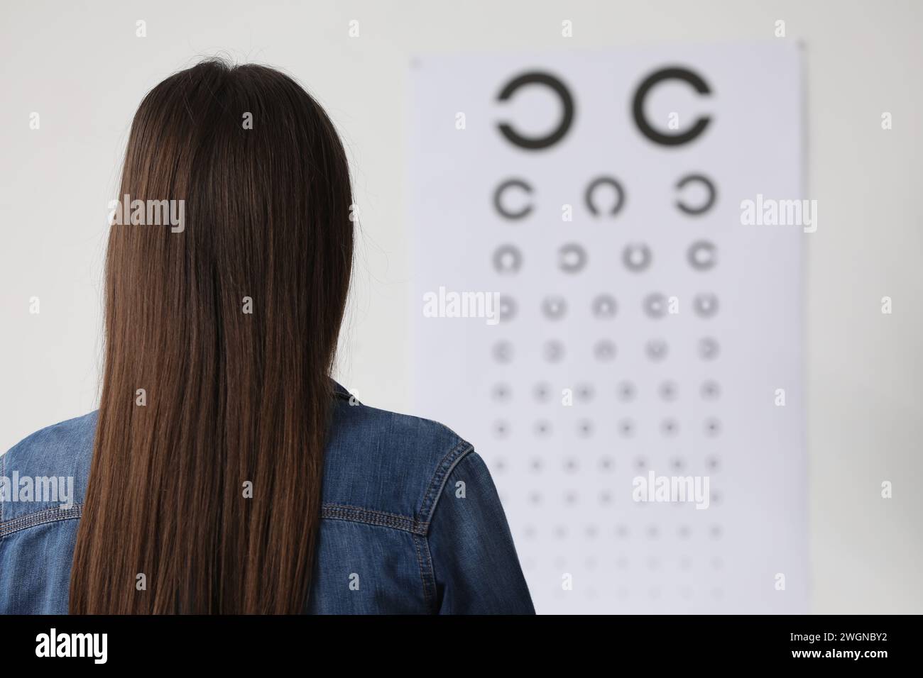 Eyesight examination. Young woman looking at vision test chart indoors ...