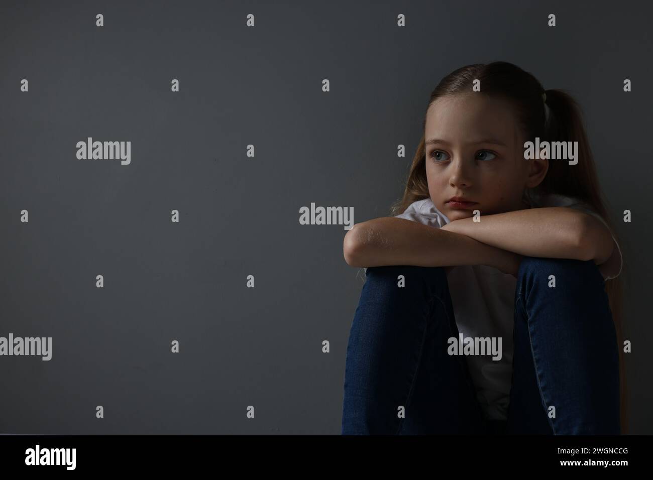 Sad girl sitting near dark grey background, space for text Stock Photo ...