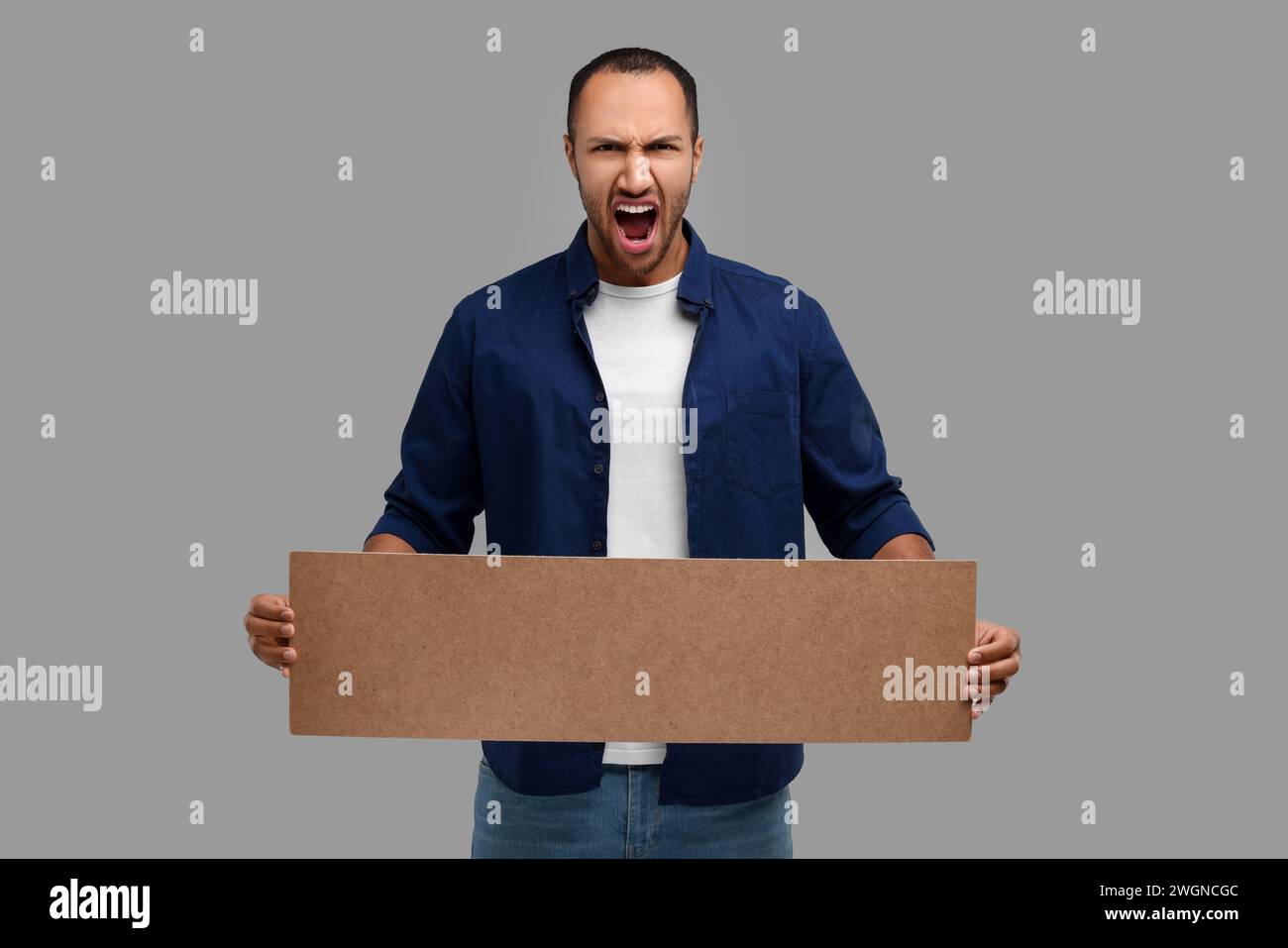 Angry man holding blank cardboard banner on grey background, space for ...