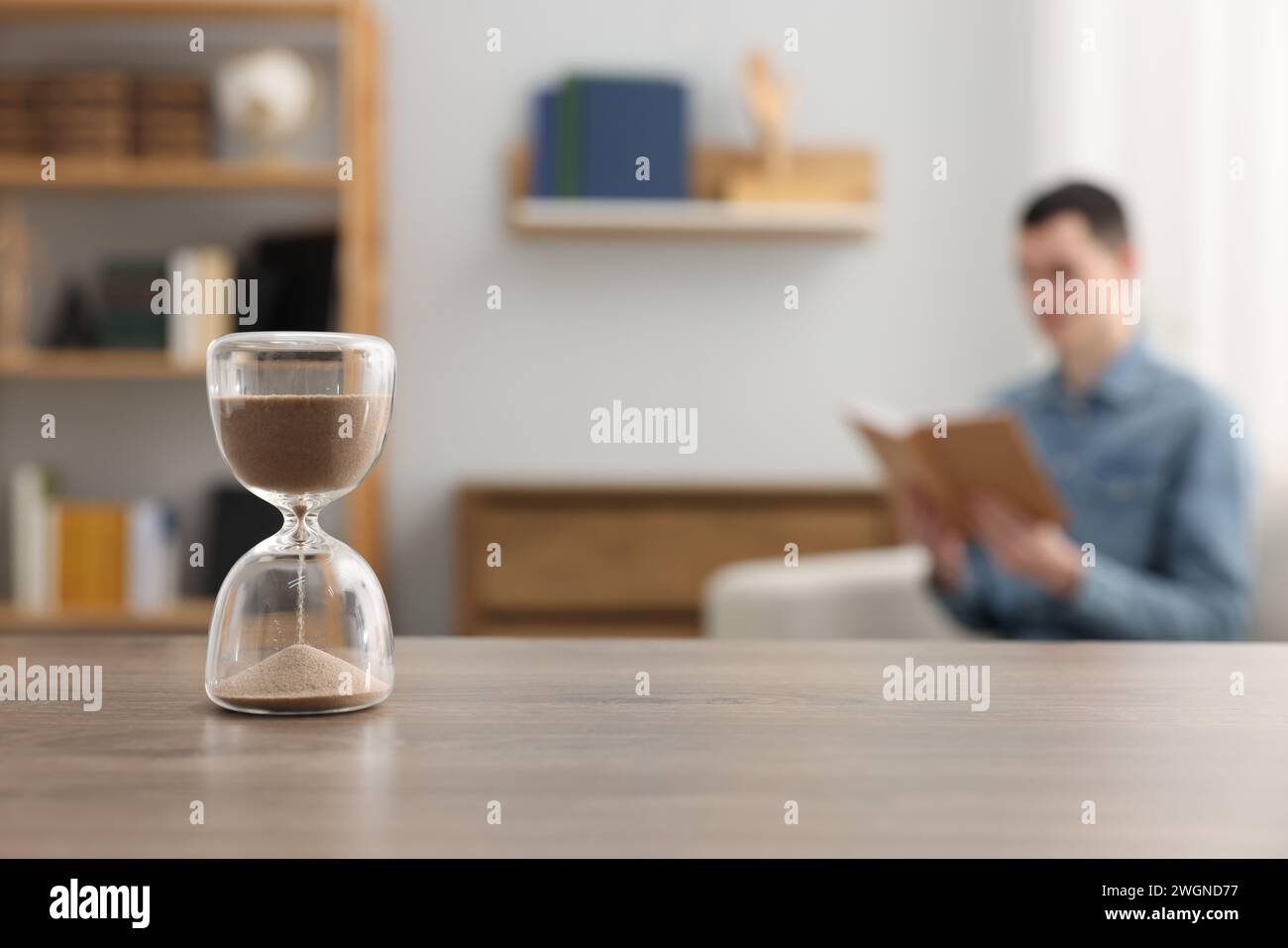Hourglass with flowing sand on desk. Man reading book in room ...