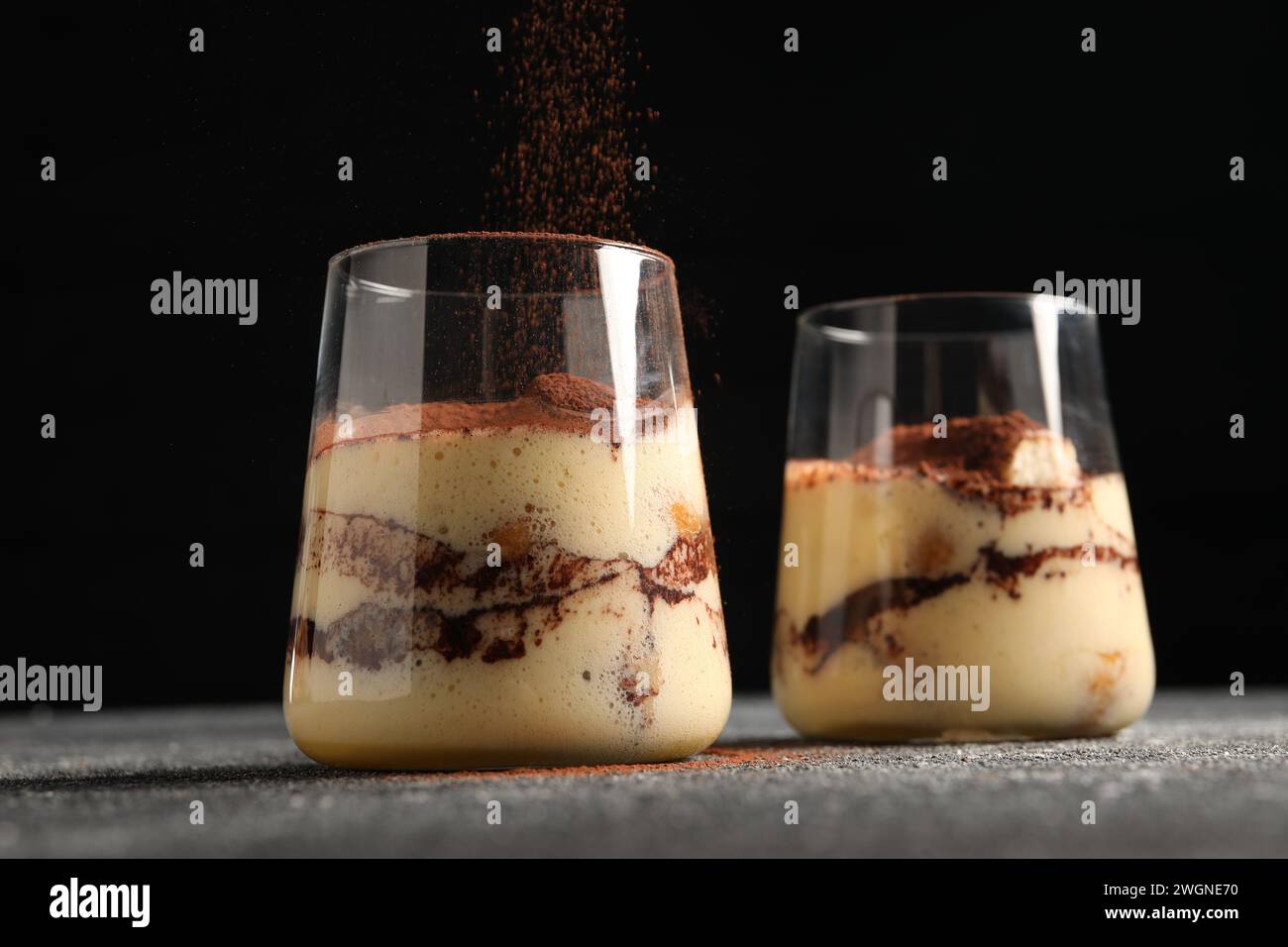 Adding cocoa powder into glass with delicious tiramisu at grey textured ...