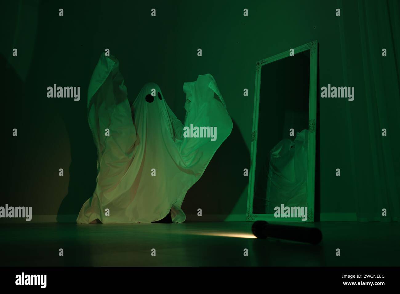 Creepy ghost. Woman covered with sheet near mirror in green light Stock ...