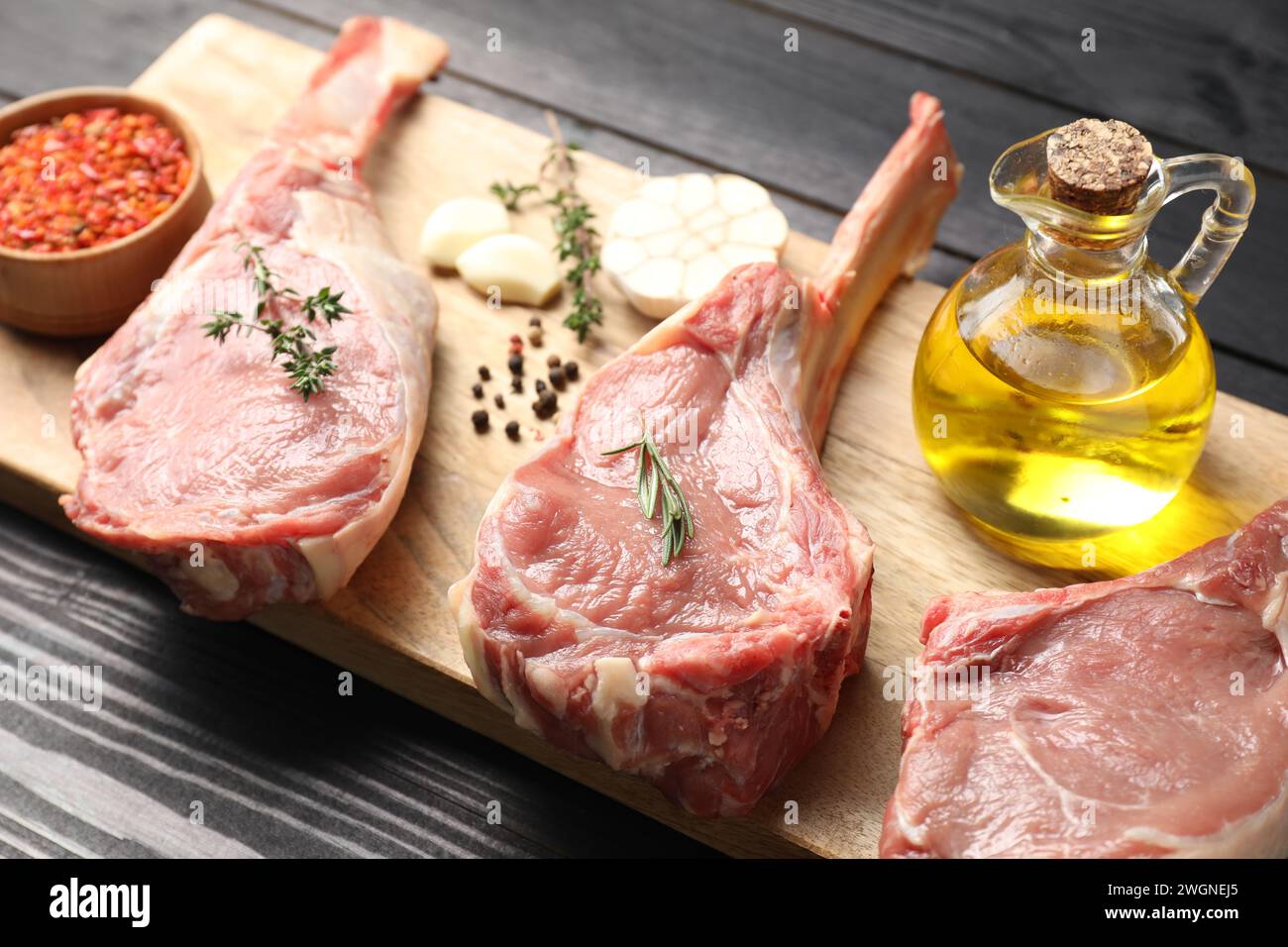 Fresh tomahawk beef cuts, spices and oil on black wooden table, closeup ...