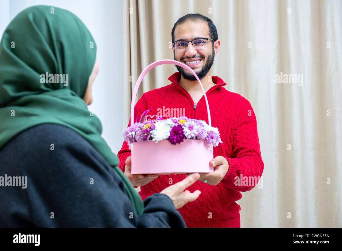 As a surprise in their home, a happy Muslim male gives roses to his ...