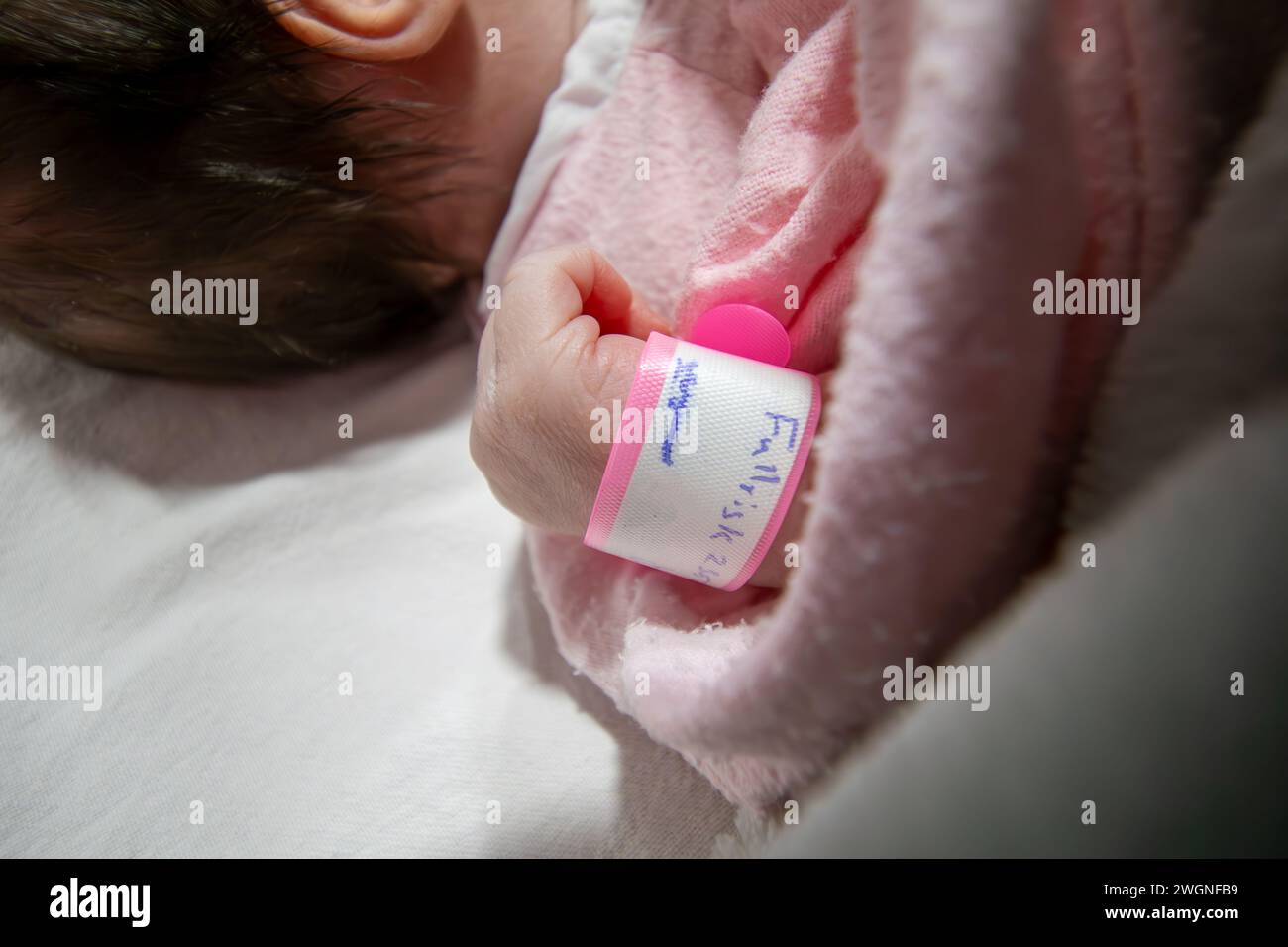 On her first day of life, a newborn baby girl wears a pink hospital ID ...