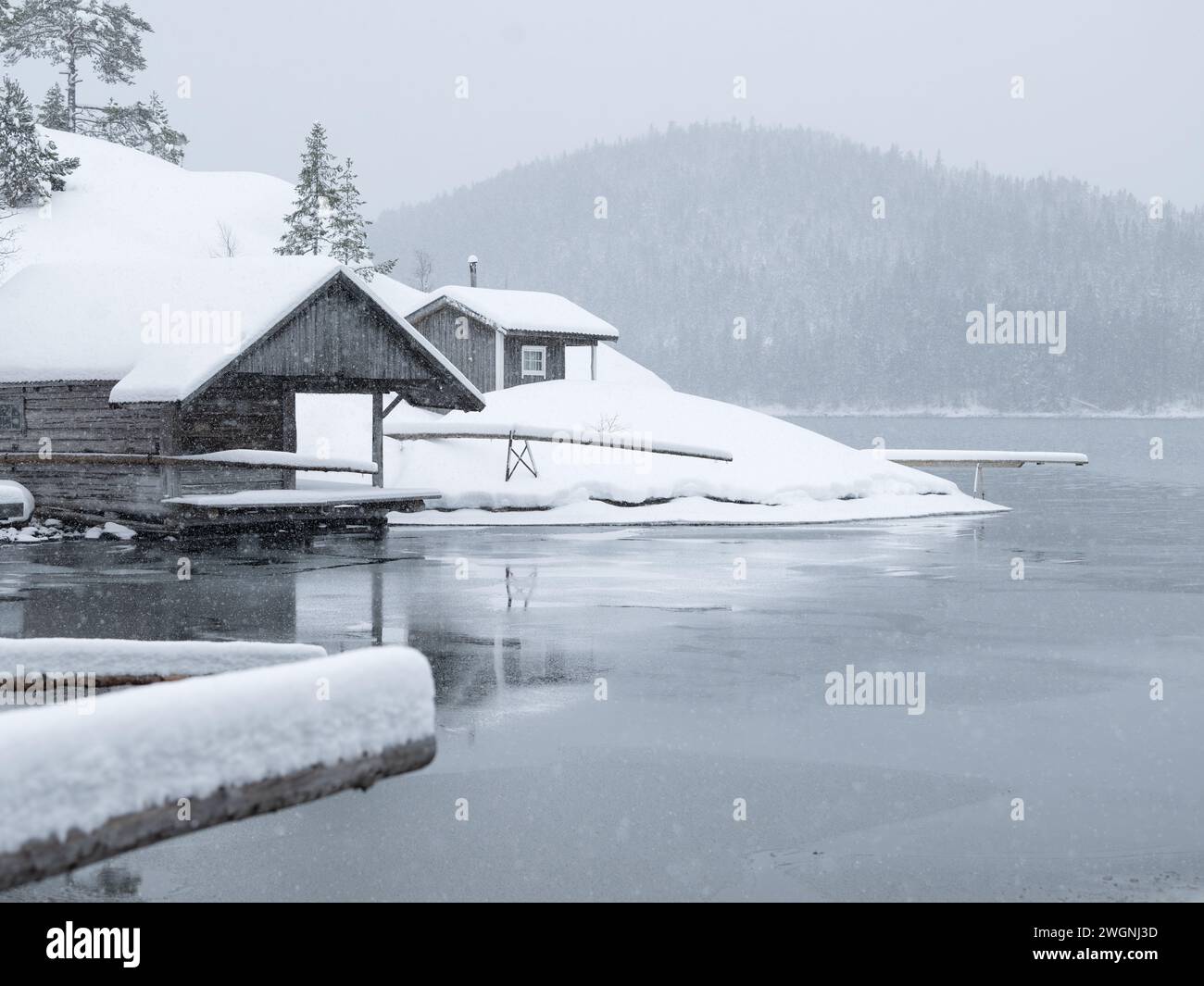 A scenic view of wooden cabins covered with snow at a lake in winter ...