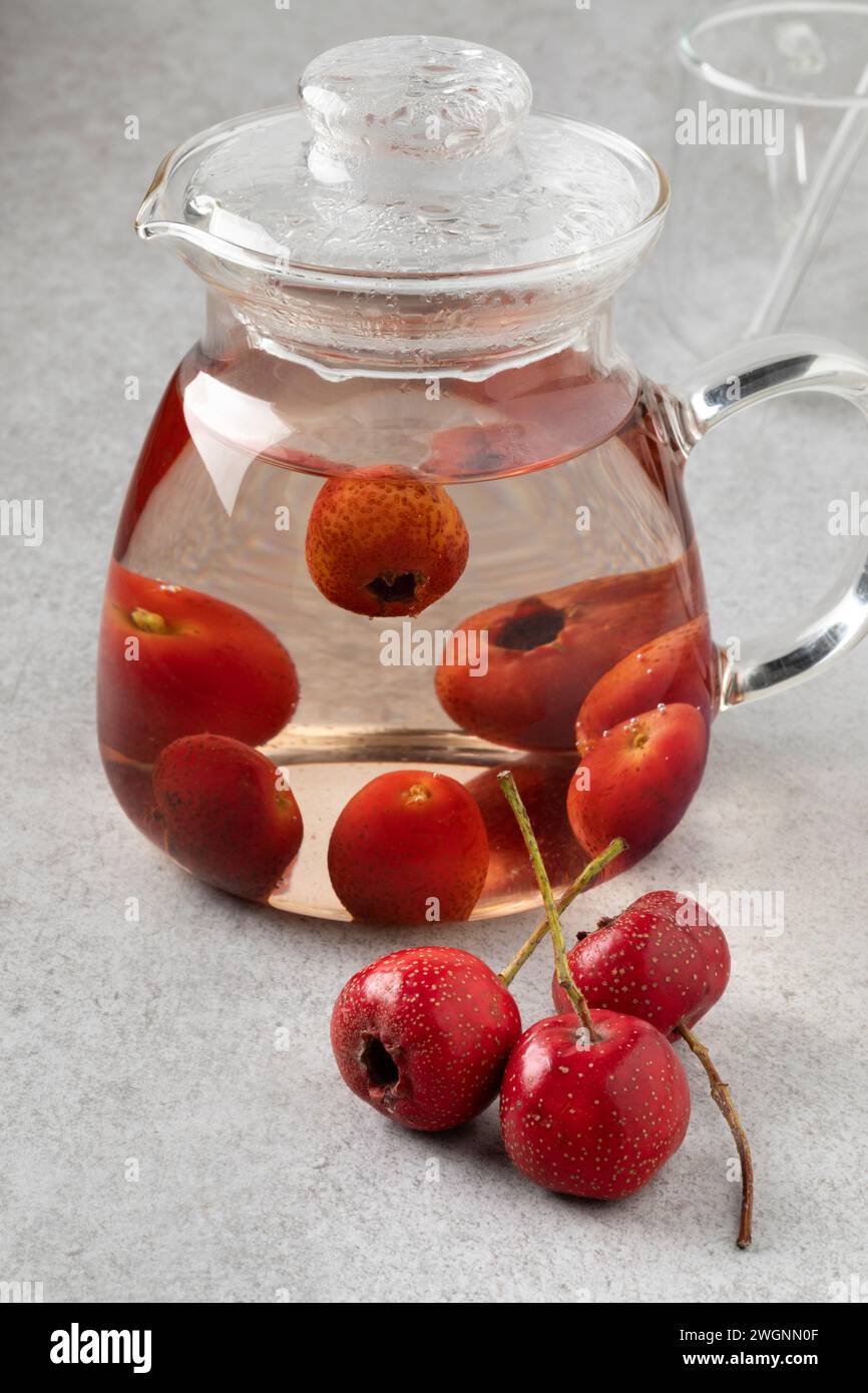 Glass teapot with red hawthorne berry tea close up and fresh hawthorne ...