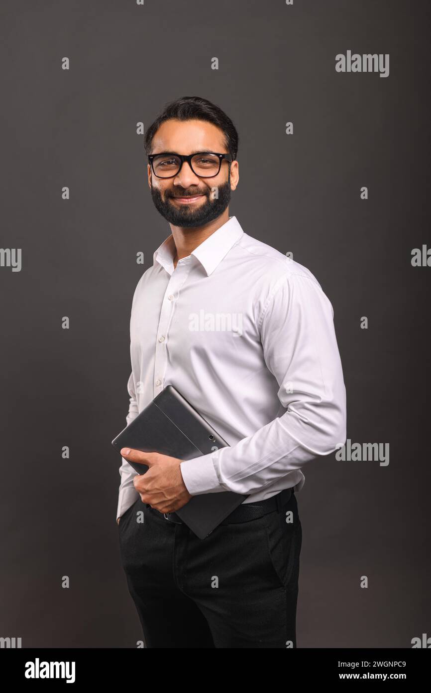 A friendly Indian businessman confidently holds a laptop, with a half ...