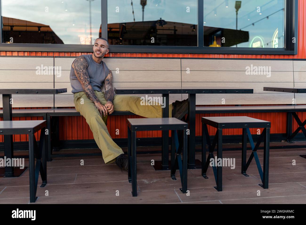A handsome young man with tattoos, sitting on a bench at an outdoor ...