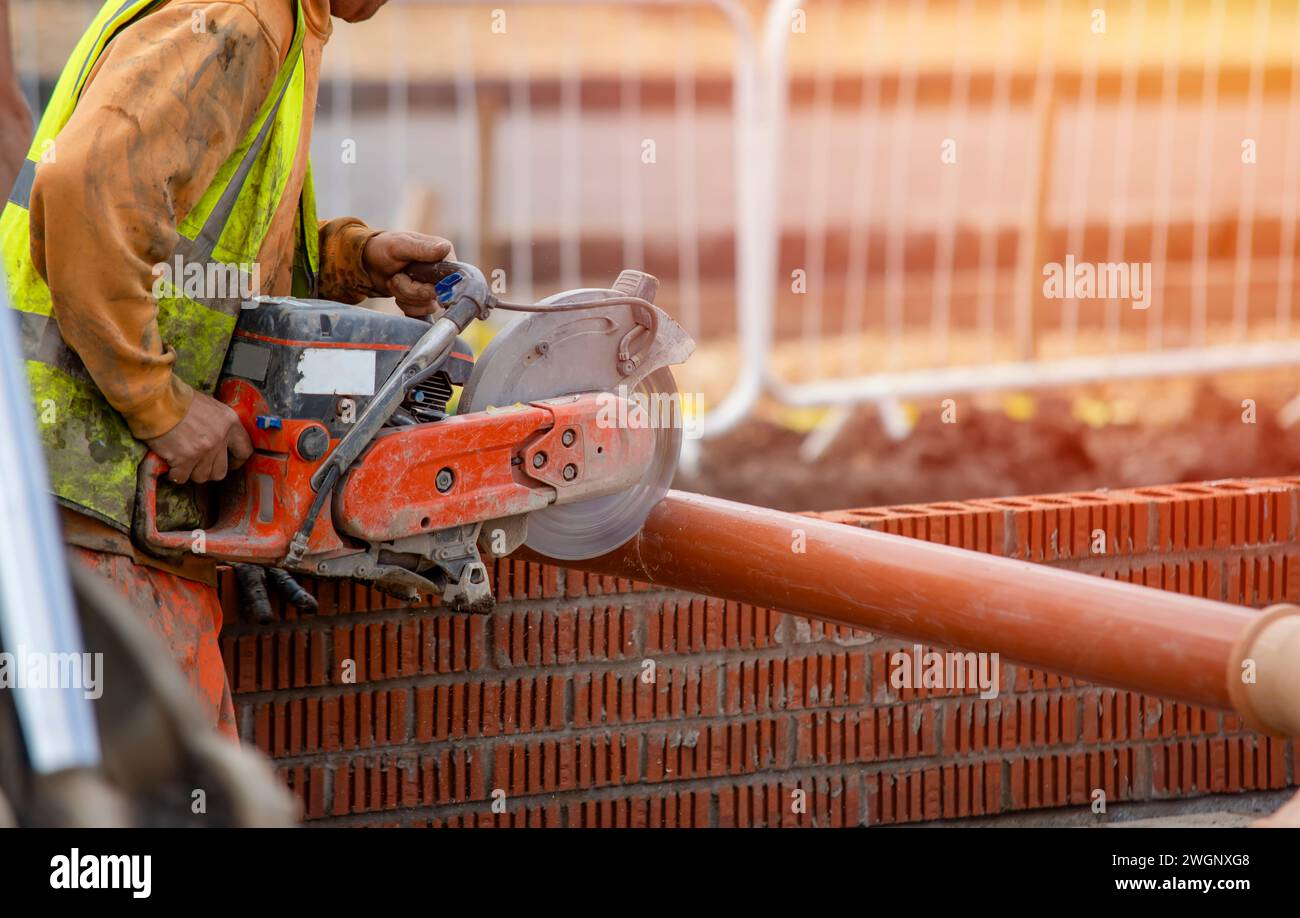 Groundworker builder cutting plastic foul drainage pipe using a petrol ...