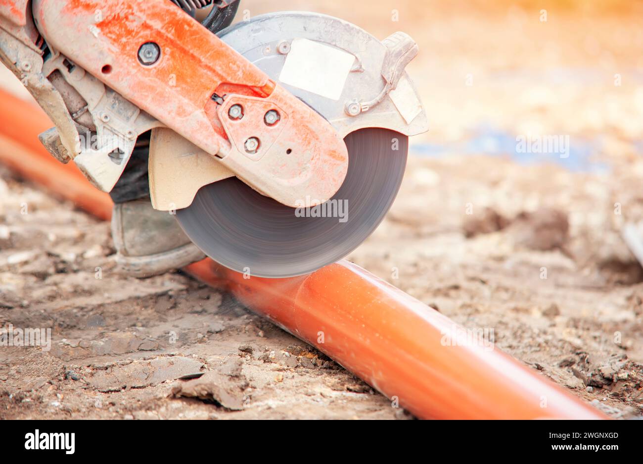 Groundworker builder cutting plastic foul drainage pipe using a petrol ...