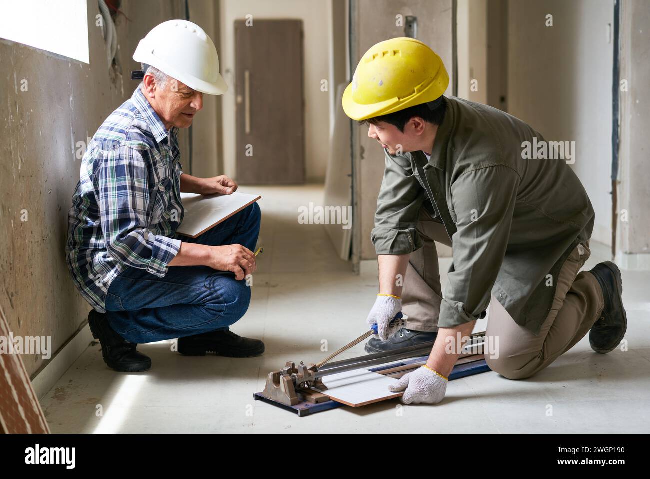 Builder crouching near worker cutting plank Stock Photo - Alamy