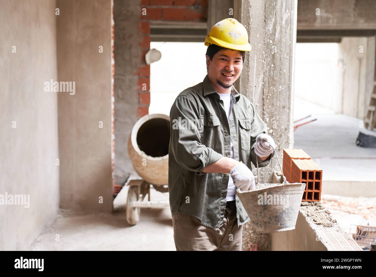 Smiling young bricklayer standing with bucket Stock Photo - Alamy