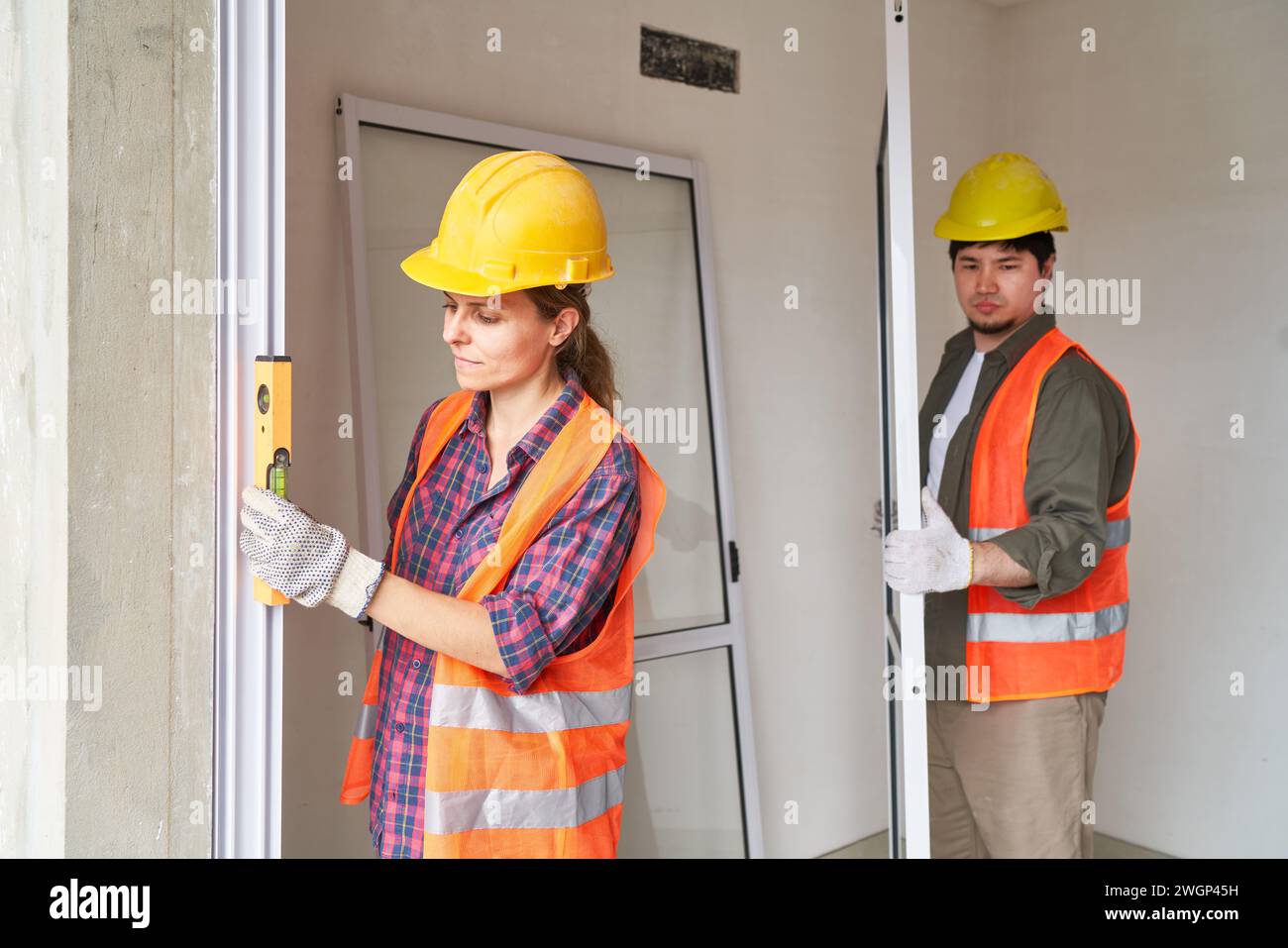 Carpenter examining frame while coworker carrying window Stock Photo ...
