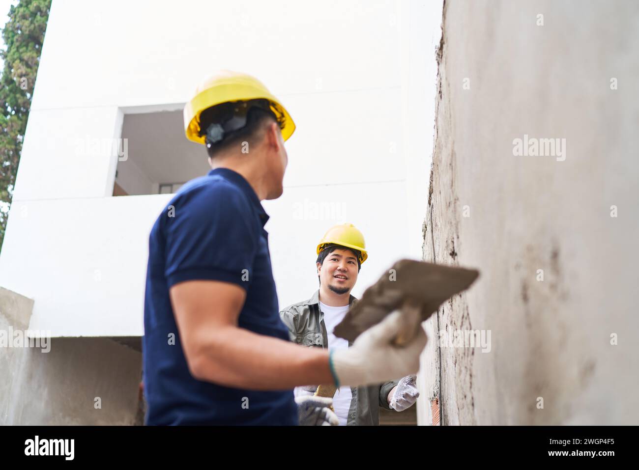 Smiling male bricklayer coworkers talking by wall Stock Photo - Alamy