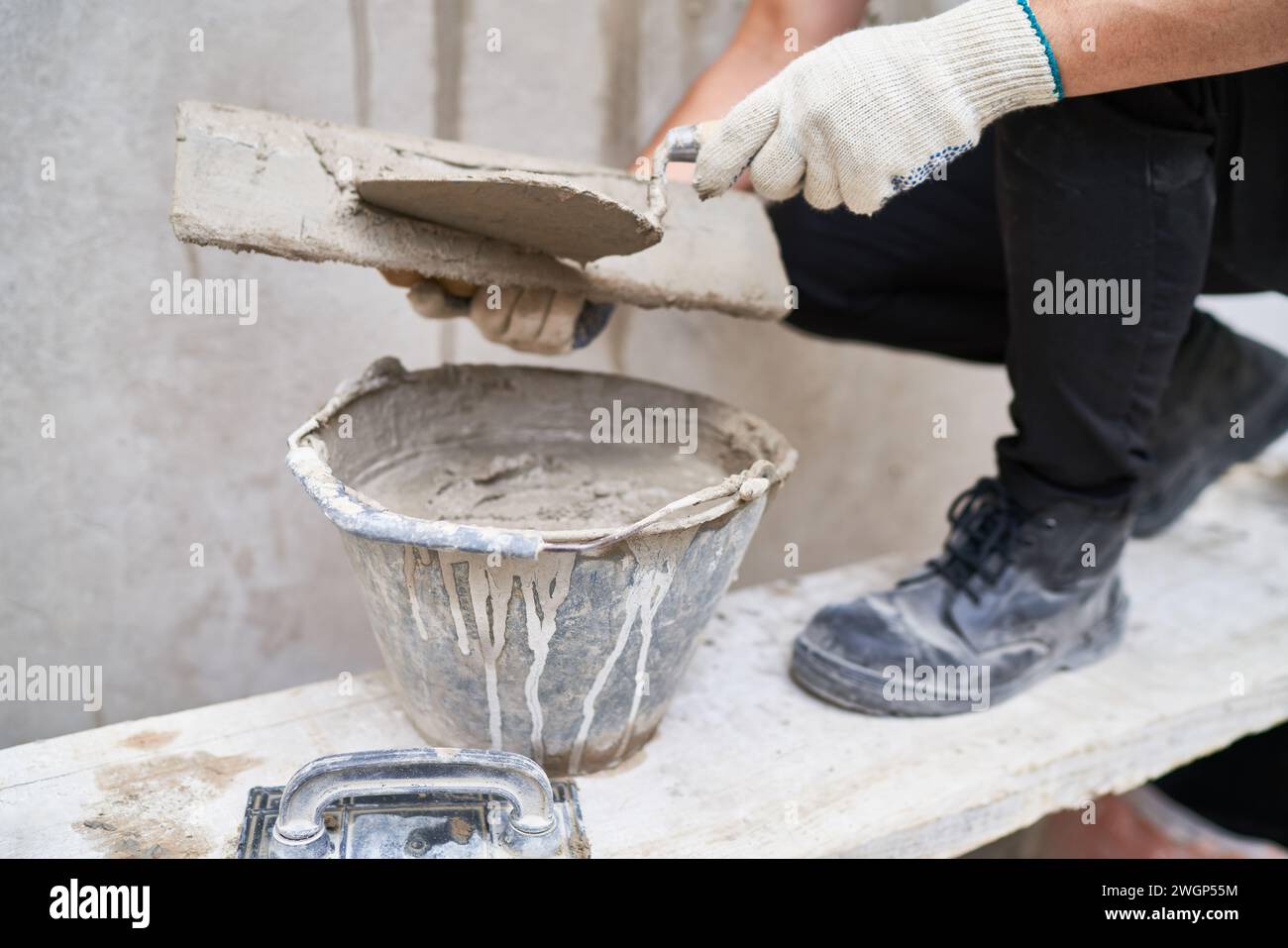 Male bricklayer taking mortar from bucket on trowel Stock Photo - Alamy