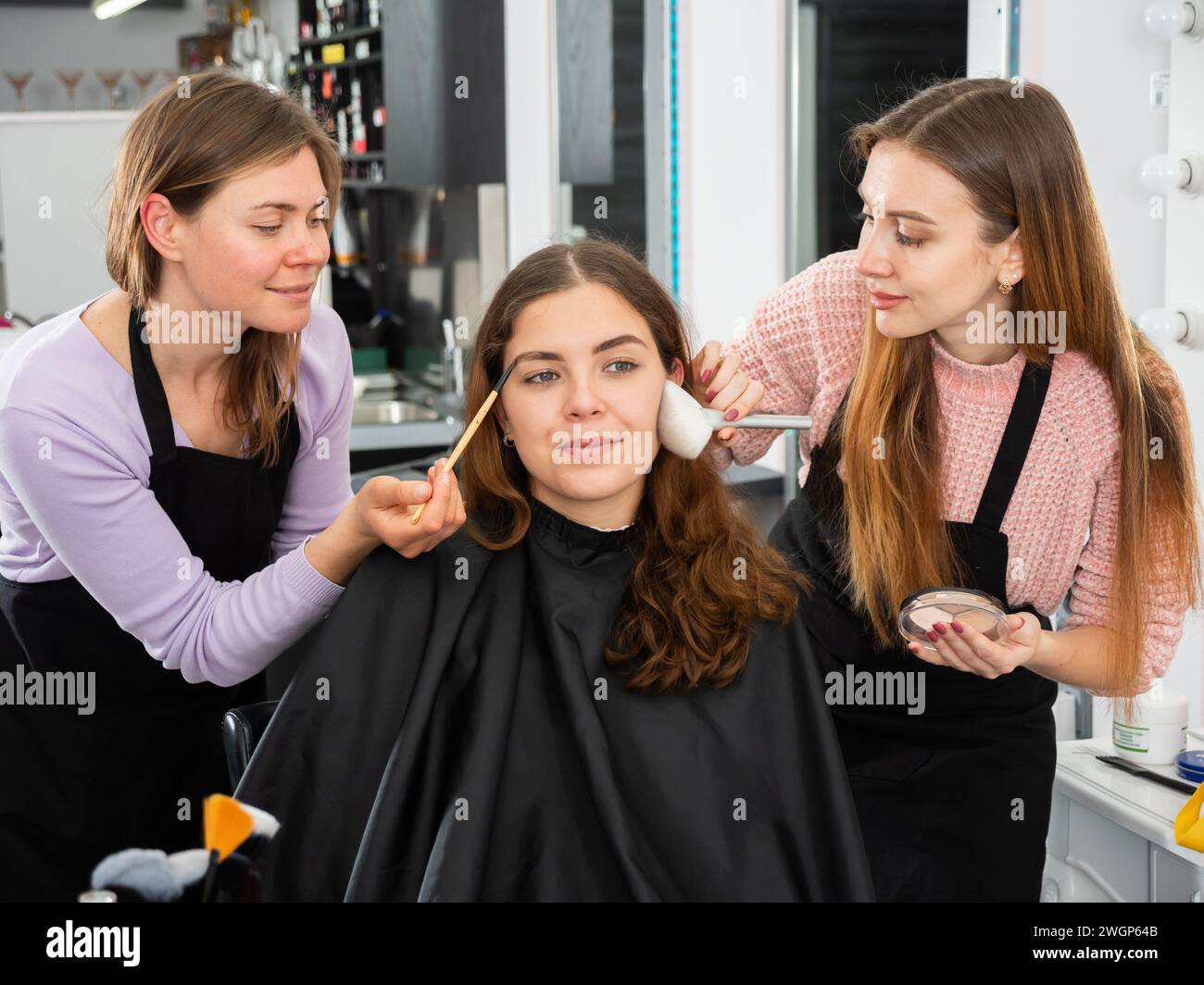 Two makeup artists apply makeup on the face of a young woman Stock ...