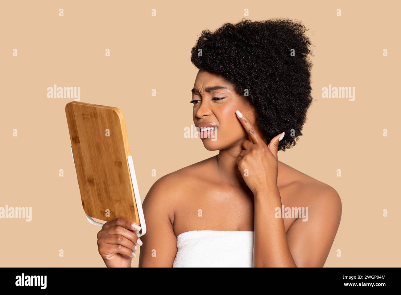 Concerned black woman examining skin with mirror, beige background ...