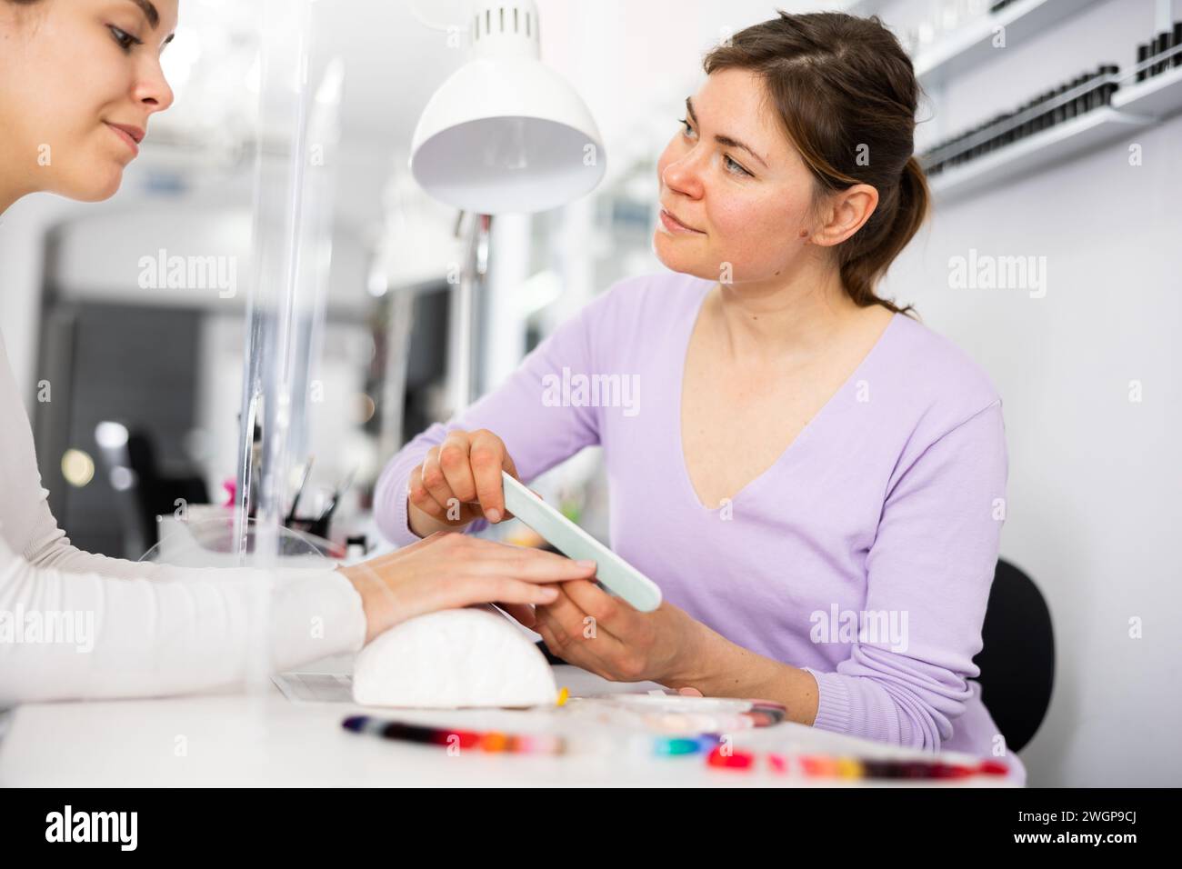 Woman manicurist filing and shaping nails of female client Stock Photo ...