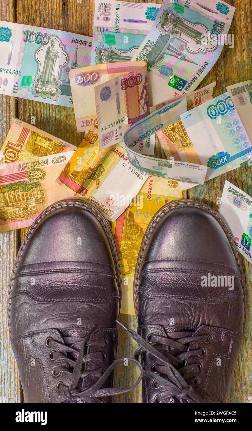 the legs of a man in black shoes stand on Russian paper money scattered ...