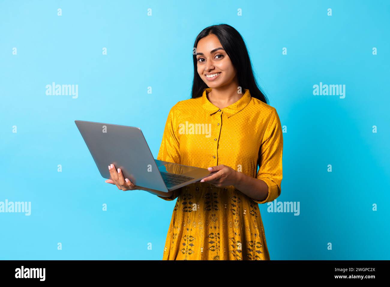 Happy middle eastern lady using laptop computer against blue backdrop ...
