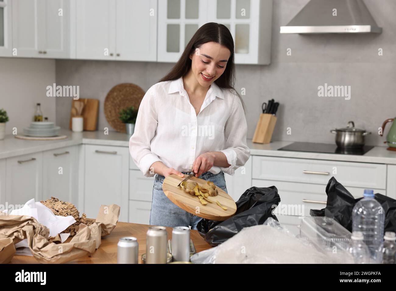 Garbage sorting. Woman putting food waste into plastic bag at table in ...