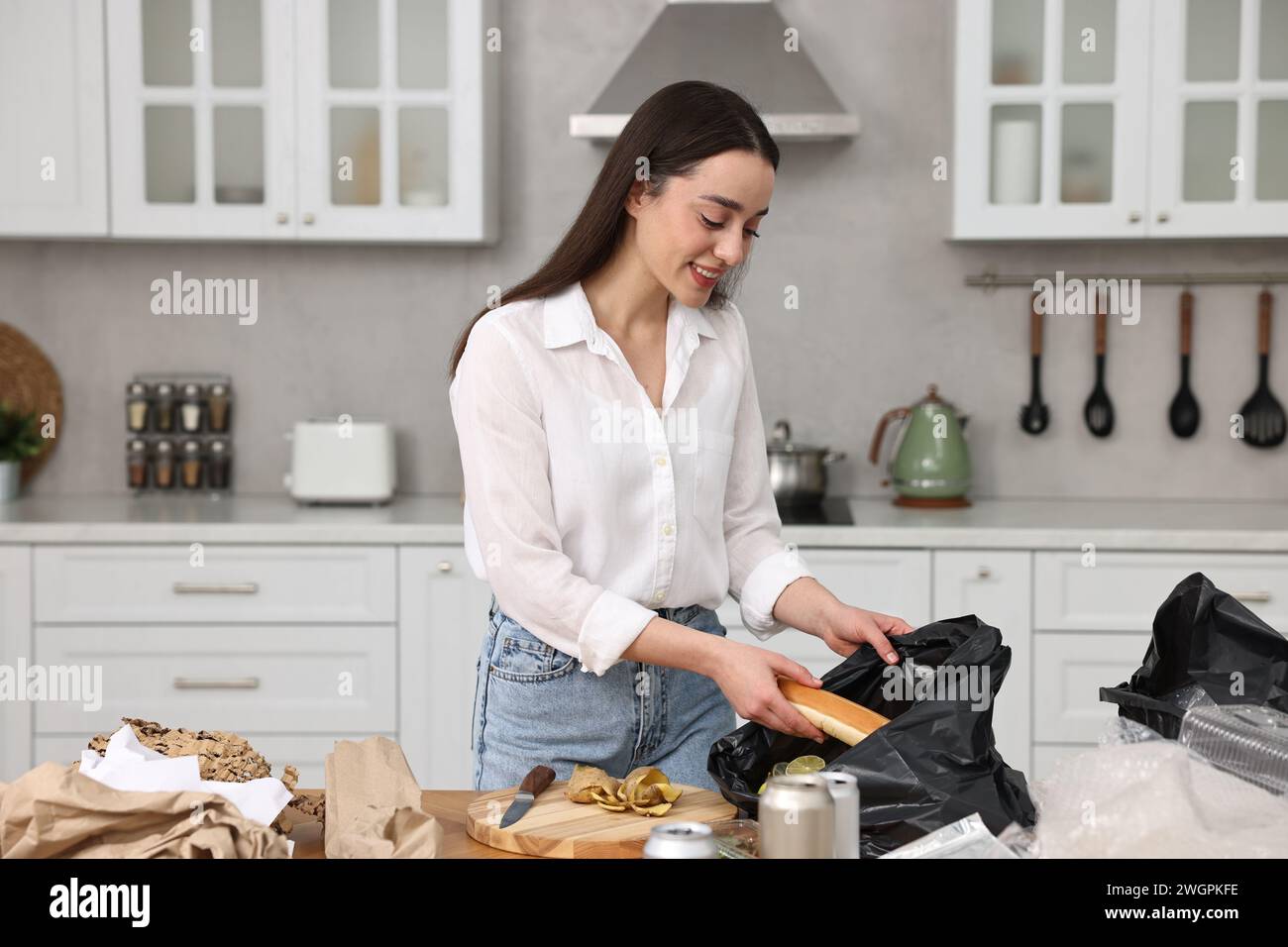 Garbage sorting. Woman putting food waste into plastic bag at table in ...
