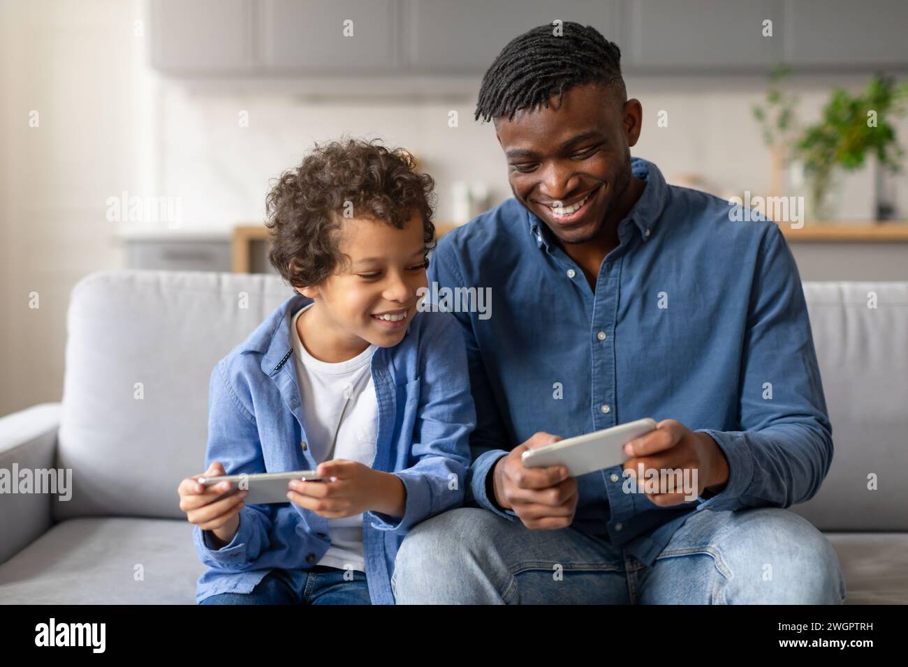 Joyful black father and son playing video games on cellphones together ...