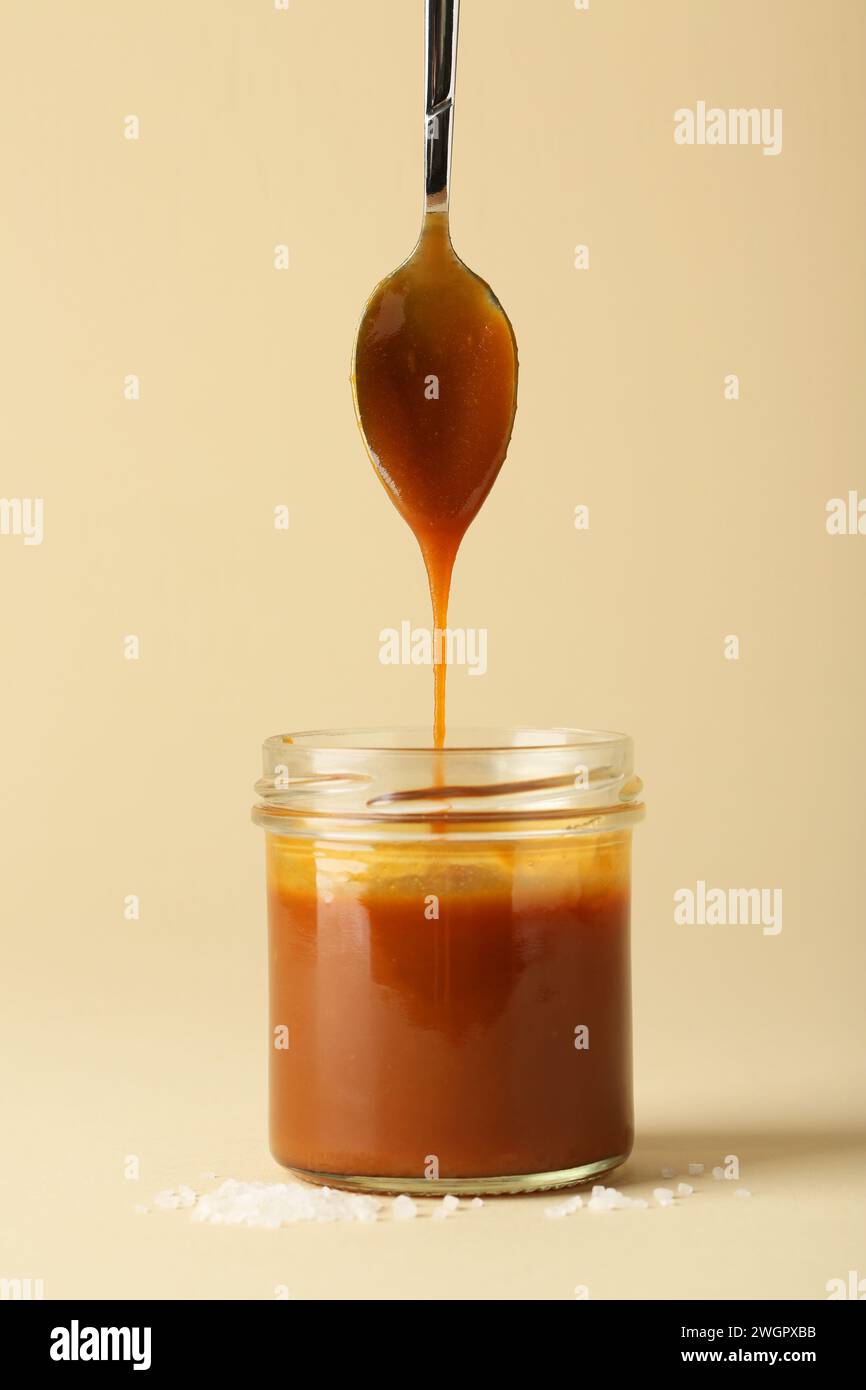 Pouring tasty salted caramel from spoon into jar on pale yellow ...