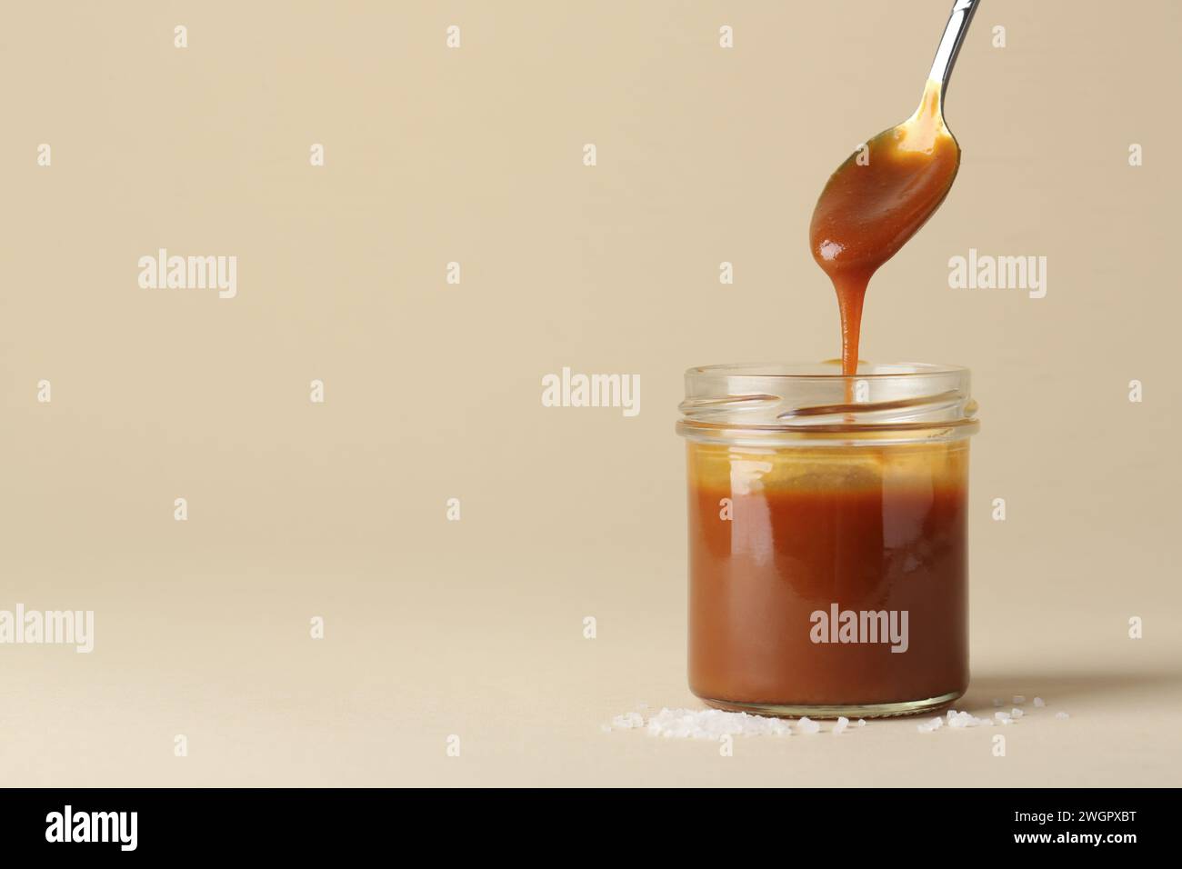 Taking tasty salted caramel with spoon from jar on pale yellow ...